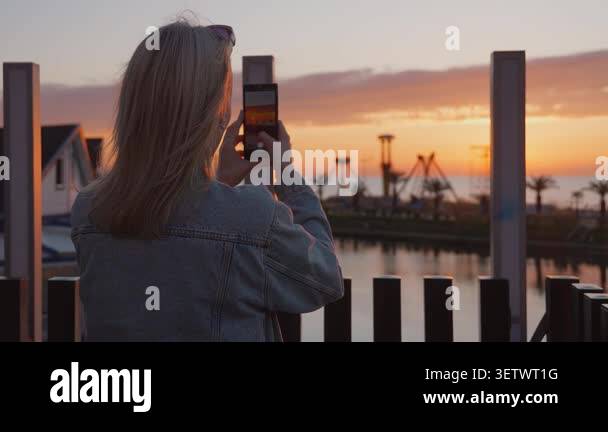 Back view of young blonde woman taking pictures of stunning orange ...