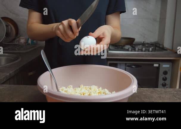 Female hands cracking a fresh chicken egg with a knife and adding it to ...
