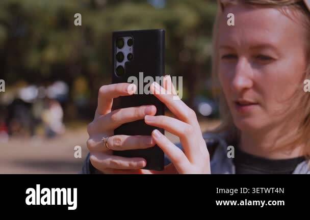 Elegant blonde woman holding a smartphone and engaging in a video call ...