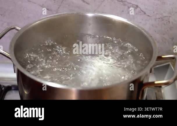 Close-up of clear water boiling vigorously with large bubbles and steam ...