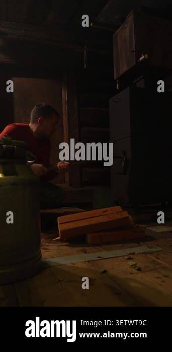 Man in a rustic wooden sauna inserting burning logs into a metal stove ...