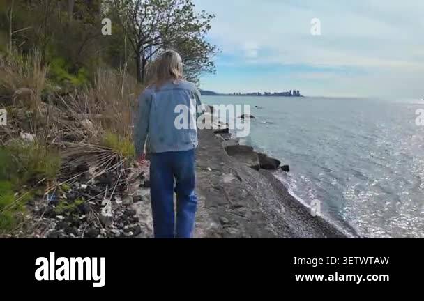 Woman wearing a denim jacket and jeans walking along a concrete ...
