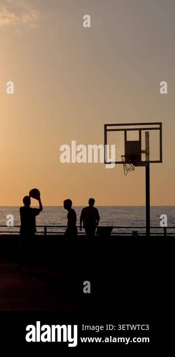 Silhouettes of young men playing streetball on a basketball court near ...