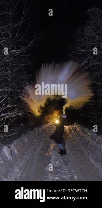 Young woman on a snowy forest road at night throwing hot water from a ...