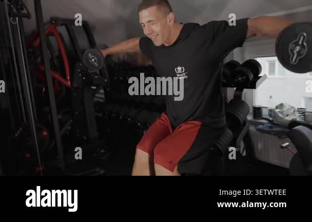 Pumped-up man is training in a gym. Bodybuilder pumping with dumbbells ...