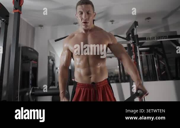 Pumped-up man is training in a gym. Bodybuilder pumping with dumbbells ...