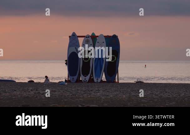 Colorful stand-up paddleboards standing on a wooden rack on a pebble ...