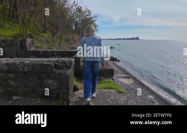 Woman wearing a denim jacket and jeans walking along a concrete ...