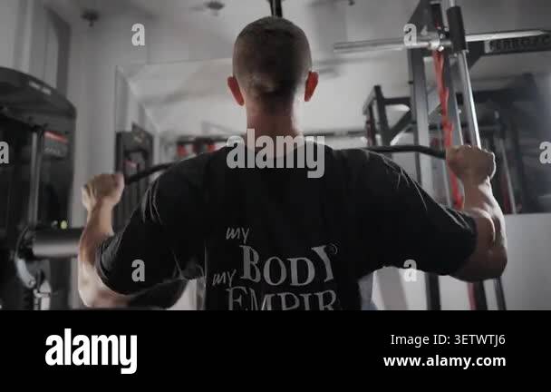 Pumped-up man is training in a gym. Bodybuilder pumping with dumbbells ...