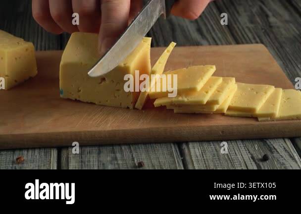 Hand positioned above yellow cheese block, slicing it into thin pieces ...