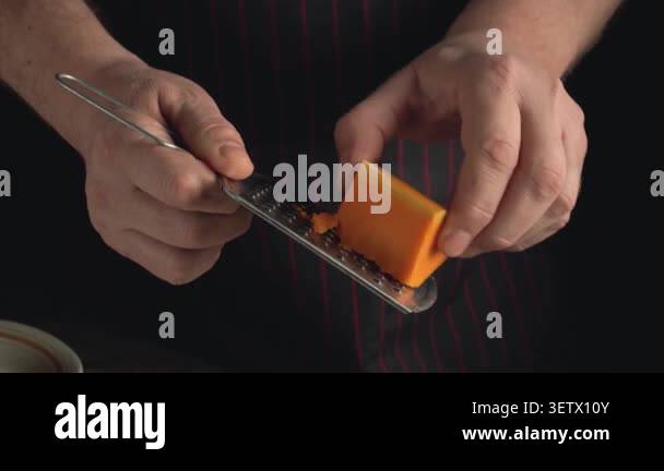 Chef grating a block of orange cheese using a metal grater, with ...