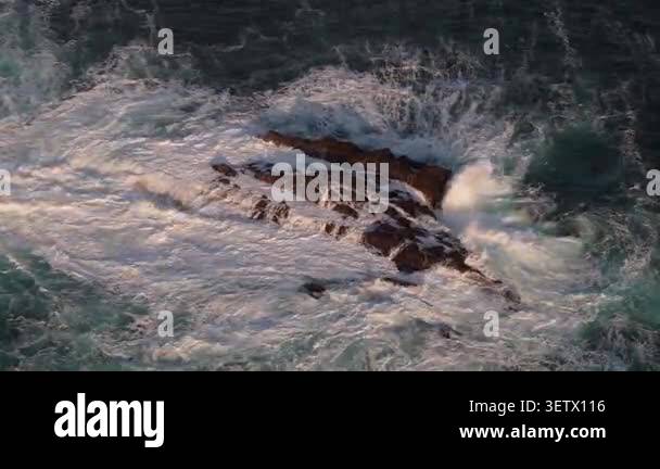 An aerial view captures the raw energy of the sea against a rocky ...
