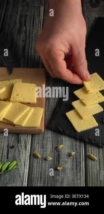 Hand is seen placing a slice of cheese onto a black slate board, while ...