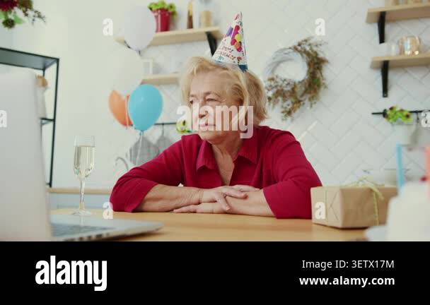 An elderly woman in a birthday hat joyfully participates in a virtual ...