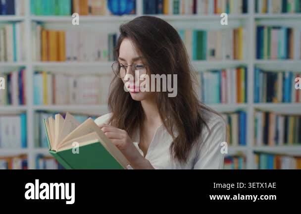 In a quiet library, a woman with glasses reads a book, surrounded by ...