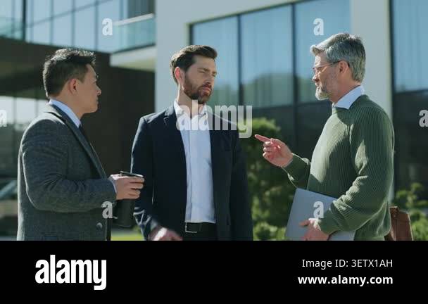 A group of professional men in suits discuss outside a modern building ...
