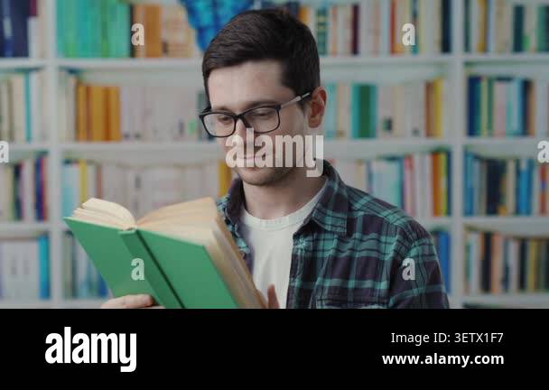 A man with glasses is engrossed in a book in a library, surrounded by ...