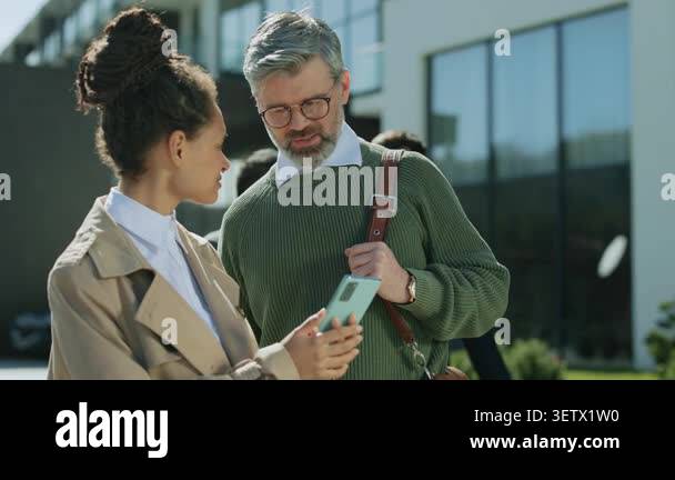 Two business people standing talking. Smiling woman showing to man ...