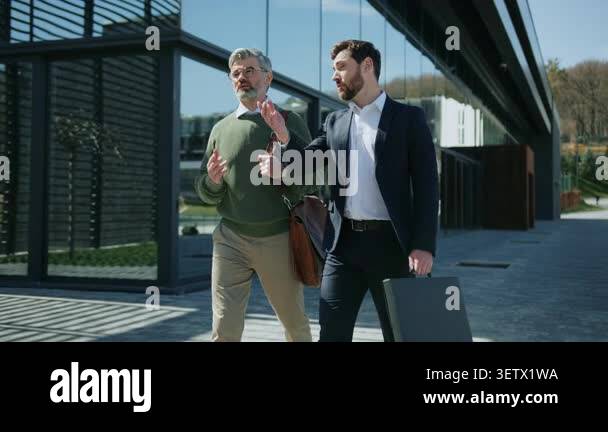 Two men in suits chat animatedly while walking down a busy street ...