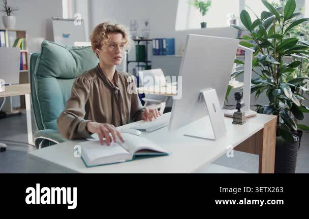 Serious good-looking Caucasian woman sitting at workplace, typing on ...