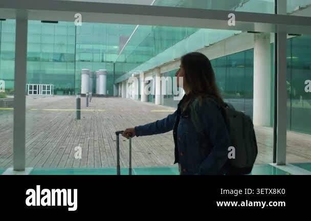 A woman walks through Barcelona airport while looking out the windows ...
