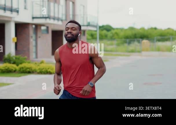 A determined man jogs in a vibrant red tank top, wearing headphones ...