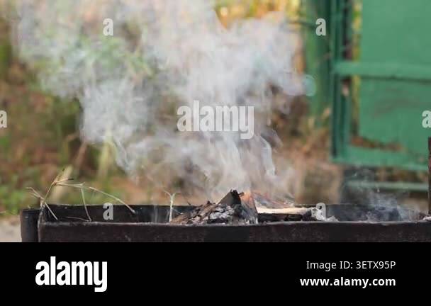 Smoldering charcoal and wood in a rusty metal barbecue grill producing ...