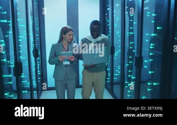 In a server room, a man and a woman analyze data on a laptop ...