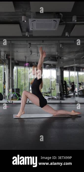 Flexible young woman practicing anjaneyasana yoga pose on a mat in a ...