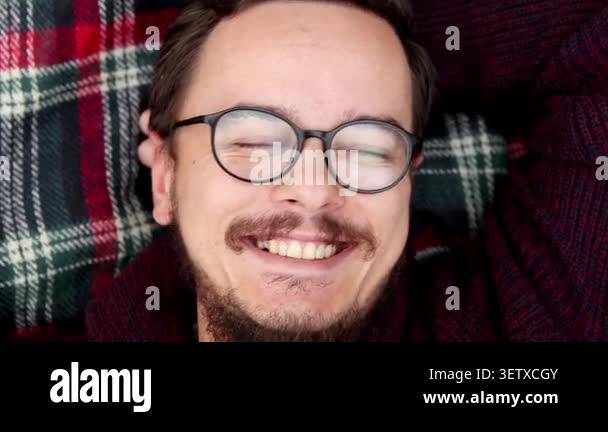 Man smiling in glasses lying on plaid blanket close up. Cozy portrait ...