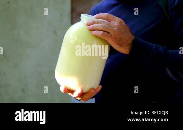 A man stands outdoors near a village house holding a large three liter ...