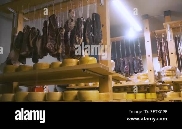 Various cuts of dried, cured meat and sausages hang above wooden shelf ...