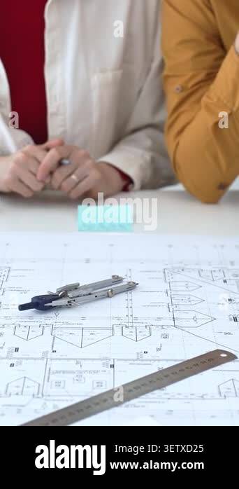 Two architects collaborate over blueprints and a white scale model ...