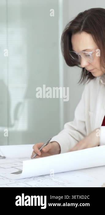 Woman working on blueprints, drawing with a pen, surrounded by design ...