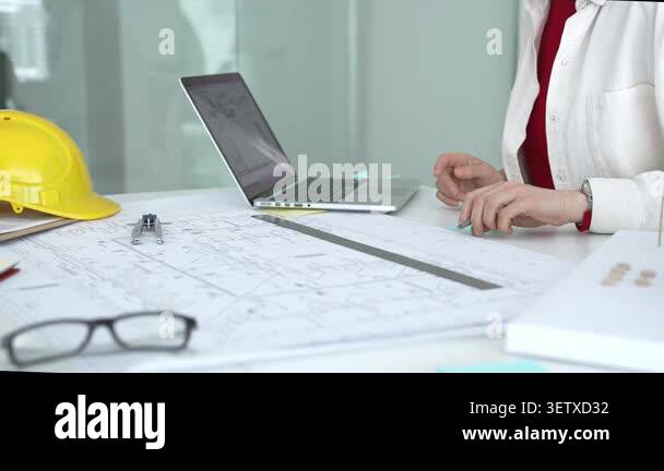 Woman working on blueprints, drawing with a pen, surrounded by design ...