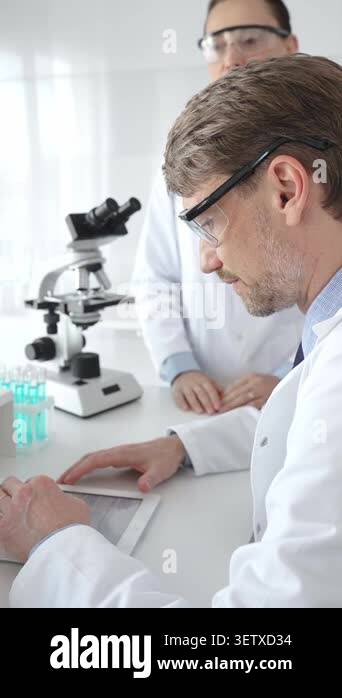 A male scientist takes notes on a tablet while his female colleague ...