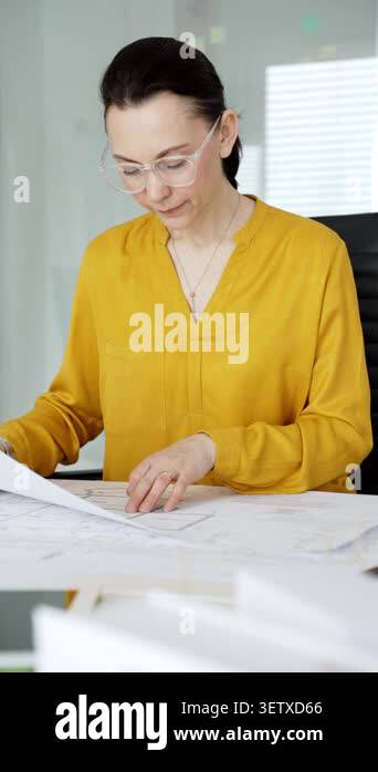 Professional woman architect in clear glasses drawing and annotating ...
