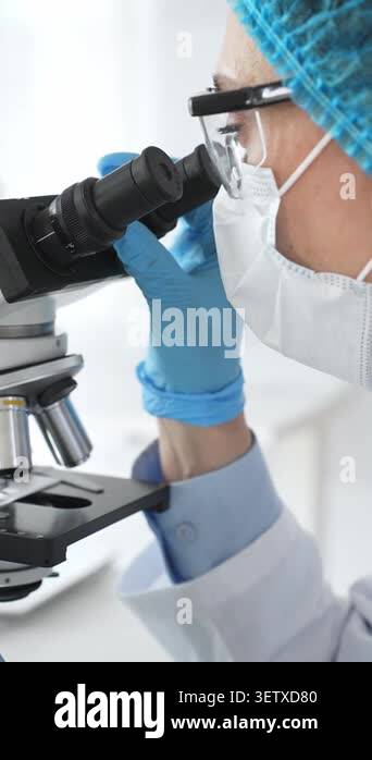 Female scientist wearing blue protective gear using a microscope ...