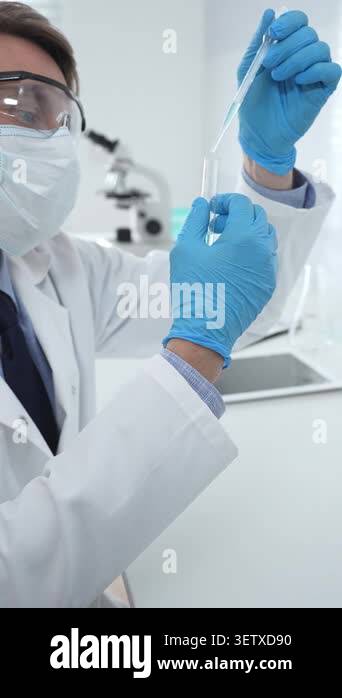 Masked male scientist in lab coat, protective glasses and blue gloves ...