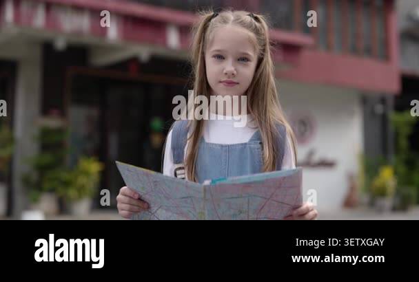 Portrait of pretty little girl holds paper map as stands on town street ...