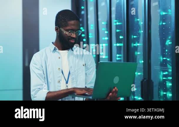 In a modern server room, a man uses a laptop, showcasing technology and ...