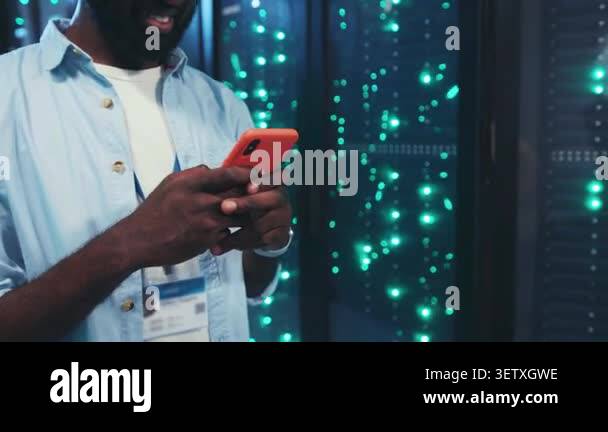 A man in a server room uses his cell phone, likely monitoring systems ...