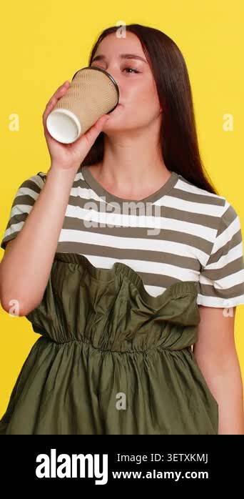 Young woman holding paper coffee cup taking a sip deeply inhaling aroma ...