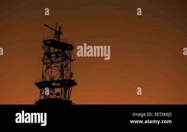 Silhouette of industrial tower structure against glowing sunset sky ...