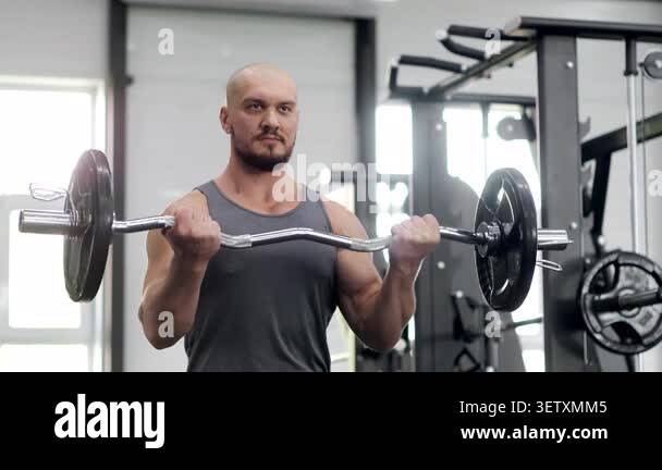 Strong male athlete performing EZ bar bicep curls in fitness gym ...