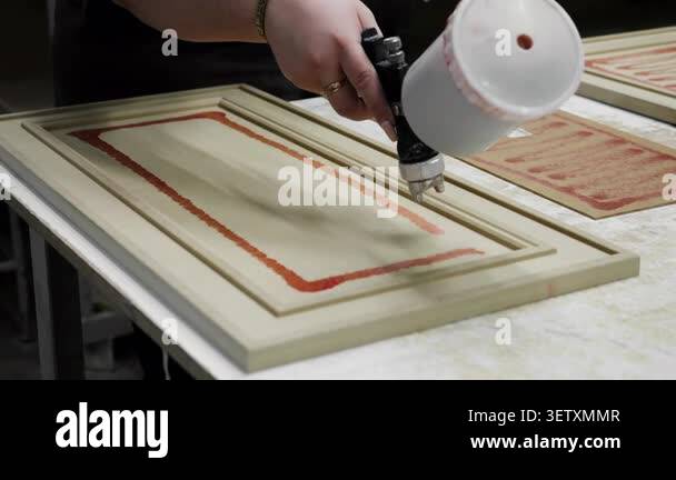Worker applying adhesive to furniture facade panel during manufacturing ...