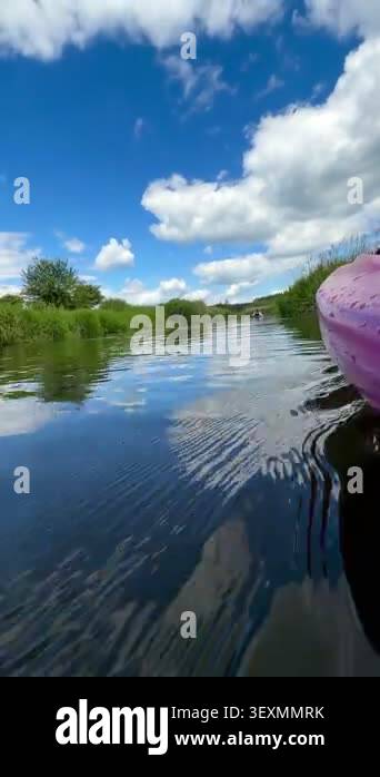 Bow of kayak moving along narrow river channel between green reeds with ...