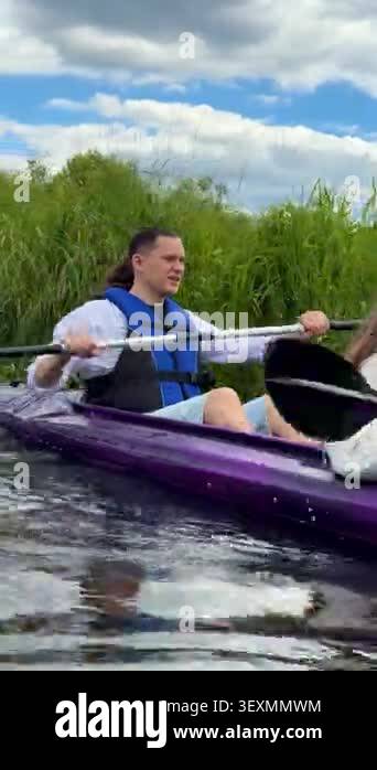 Father and daughter paddling kayak along narrow river surrounded by ...