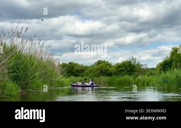 Family wearing life jacket kayaking along calm river during summer day ...