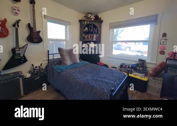A cozy bedroom scene showing a bed with a blue blanket, guitars on the ...